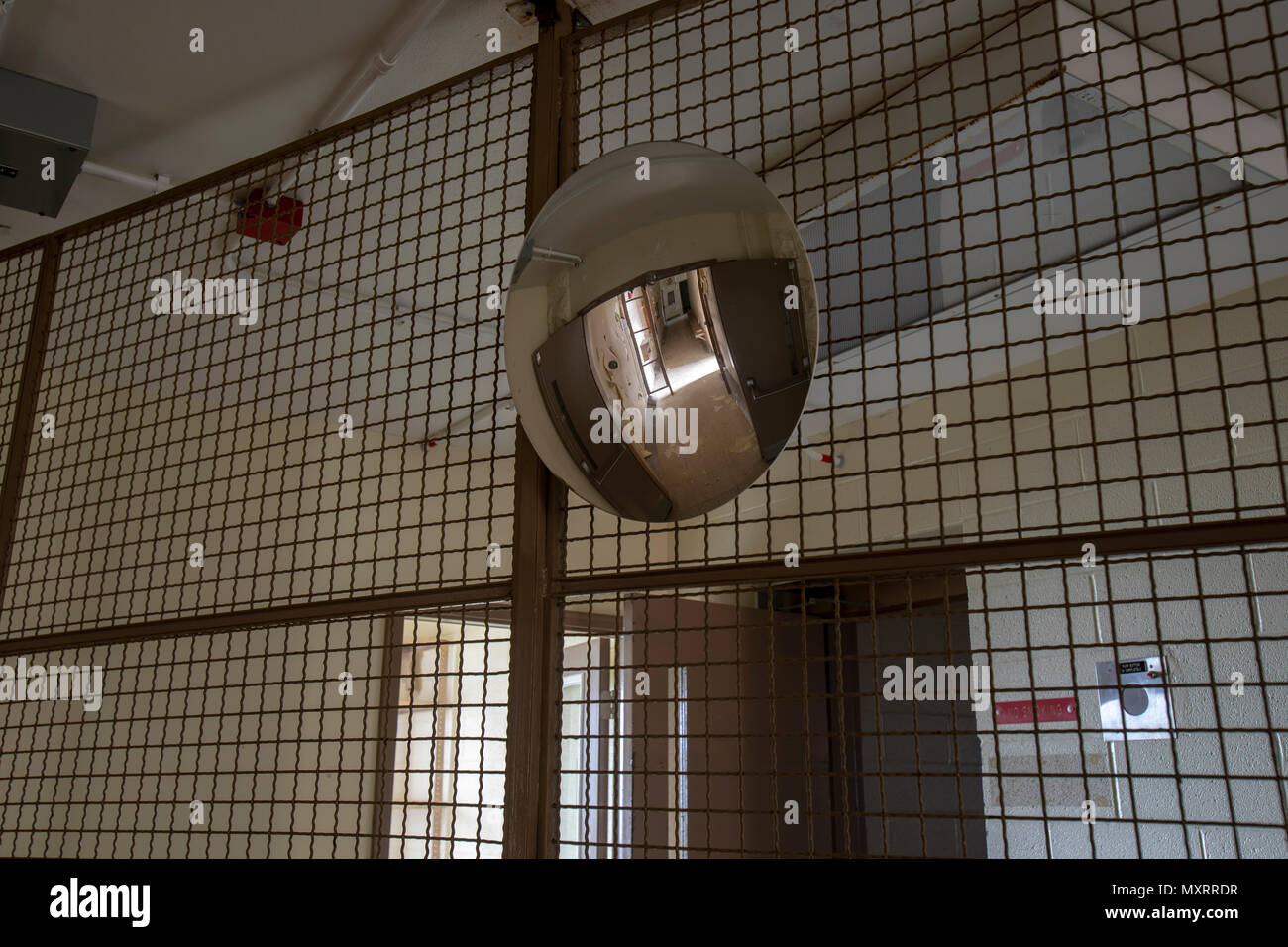 Security mirror on metal grate reflecting gates in doors in hallway of ...