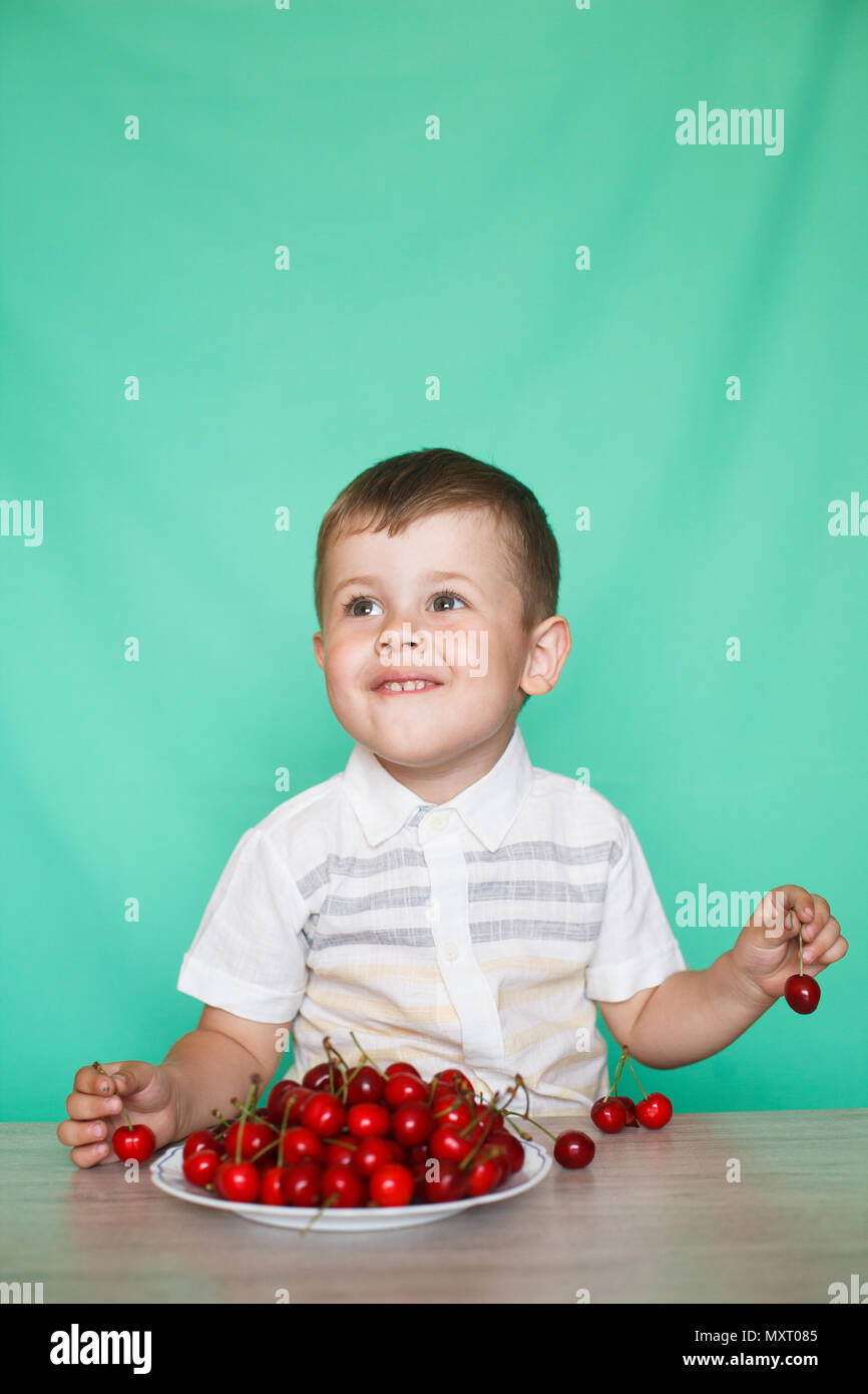 Cute boy boy eating ripe cherries, making funny faces and playing with ...