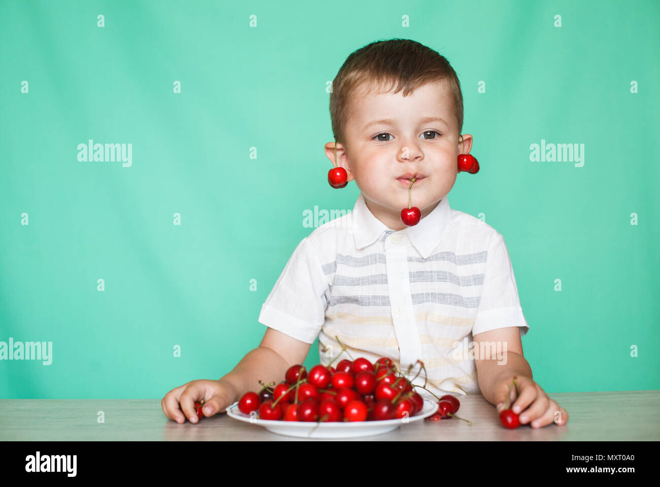 Cute boy boy eating ripe cherries, making funny faces and playing with ...