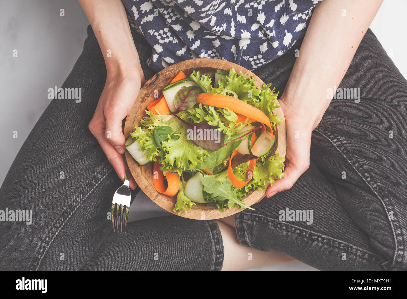 The woman in black jeans eating summer vegetable salad in a wooden bowl ...
