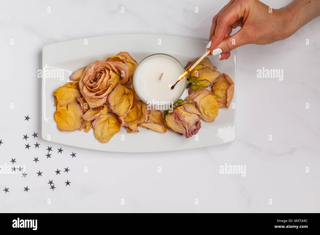 Beautiful white flat lay with a candle and dried rose petals. Top view ...