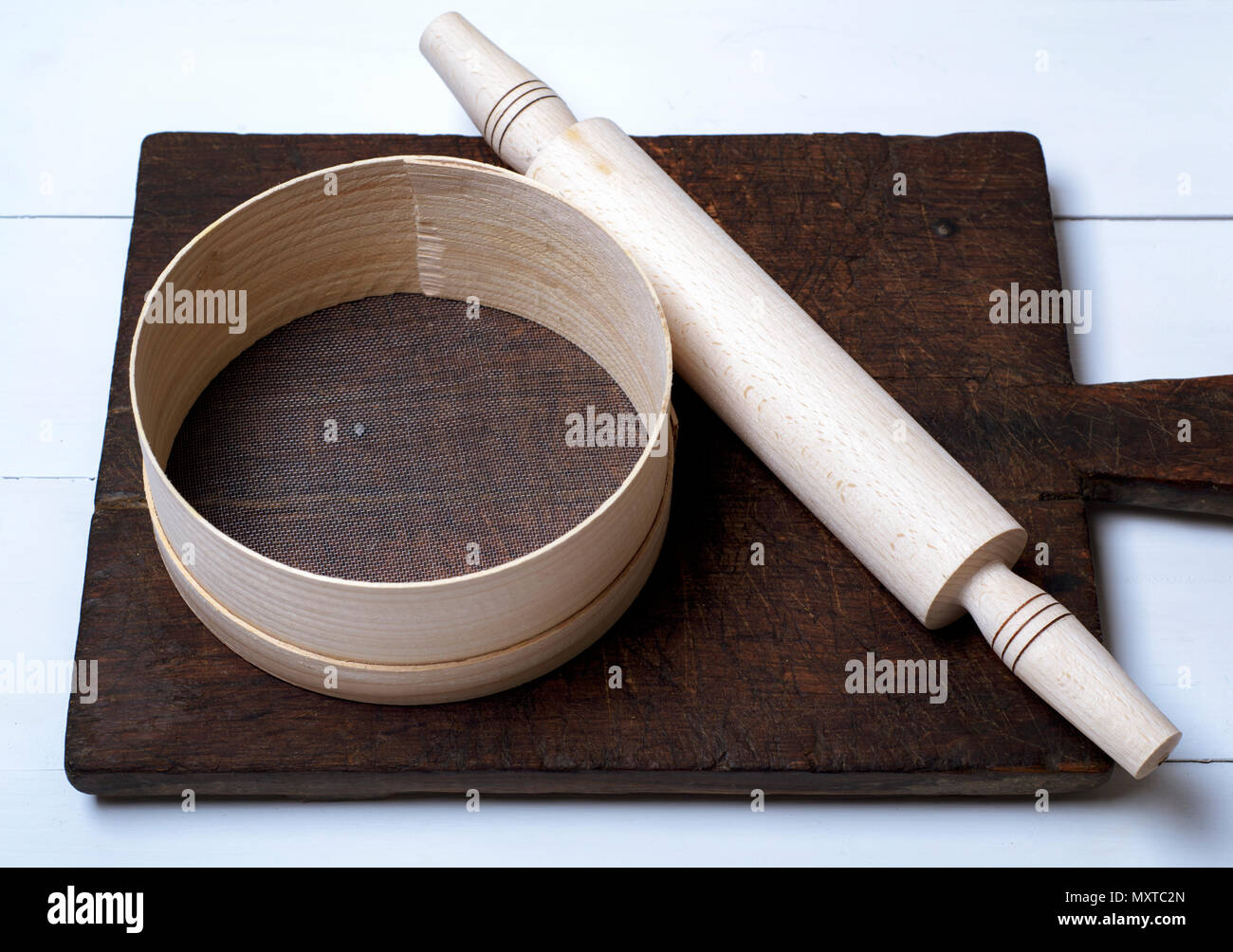 brown wooden kitchen cutting board, rolling pin and sieve on a white ...