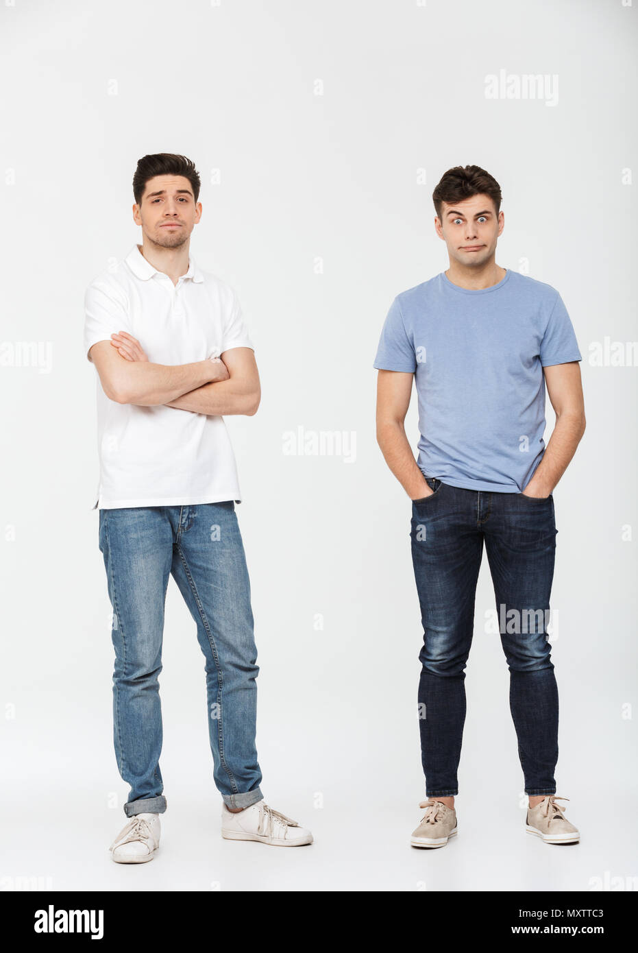 Full length portrait of two confused young men looking at camera ...