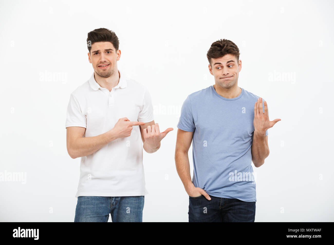 Portrait of two confused young men pointing fingers isolated over white ...