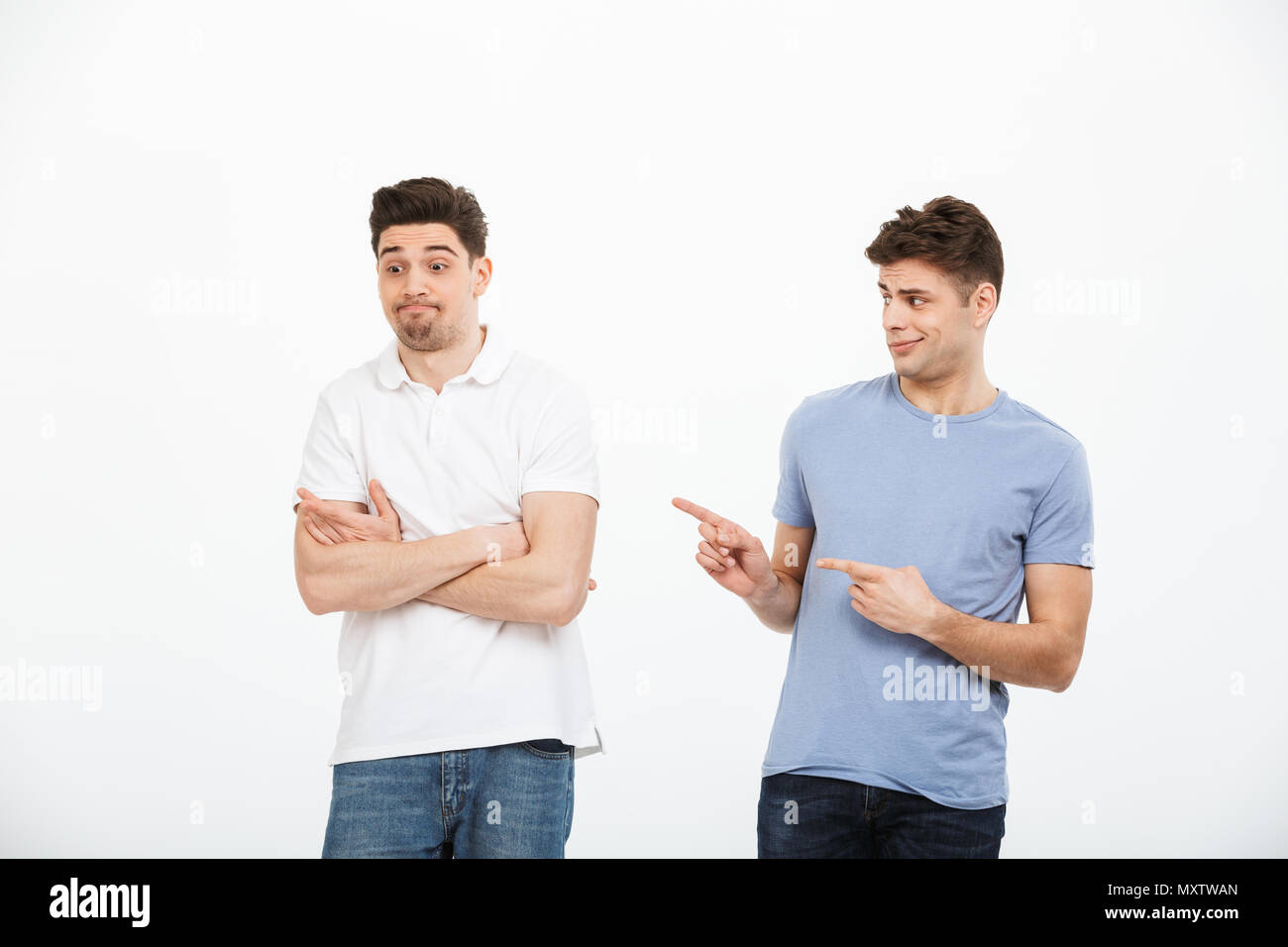 Portrait of two puzzled young men pointing fingers isolated over white ...