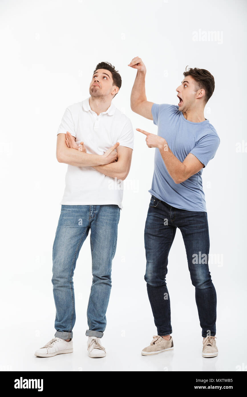 Full length portrait of two confused young men pointing fingers ...