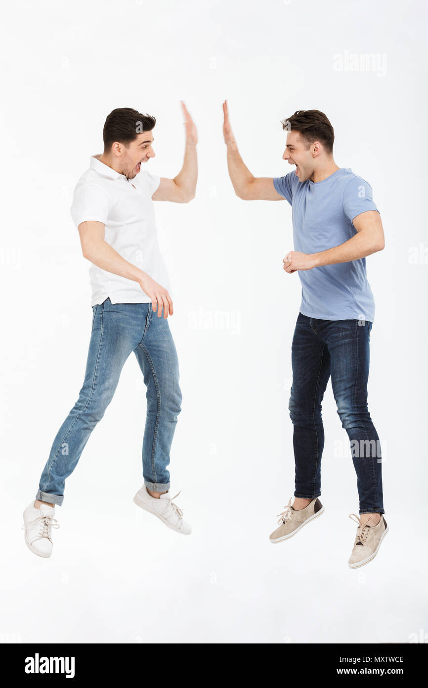 Full length portrait of two happy young men giving high five isolated ...