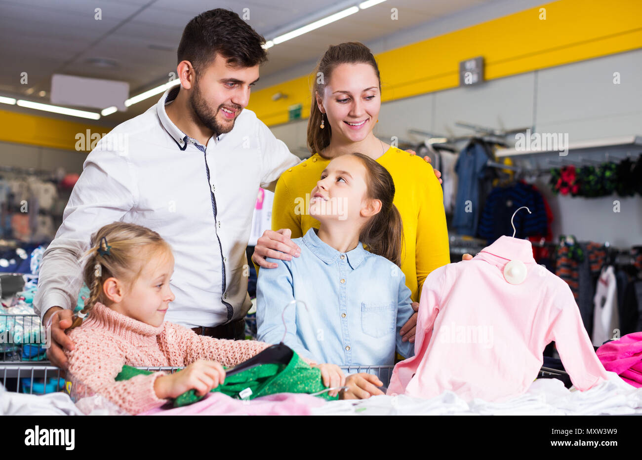 smiling young family with two girls choosing new clothes in mall Stock ...