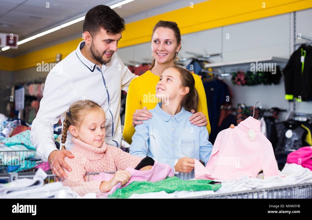 Young smiling family of four looking for children clothes on shelves in ...