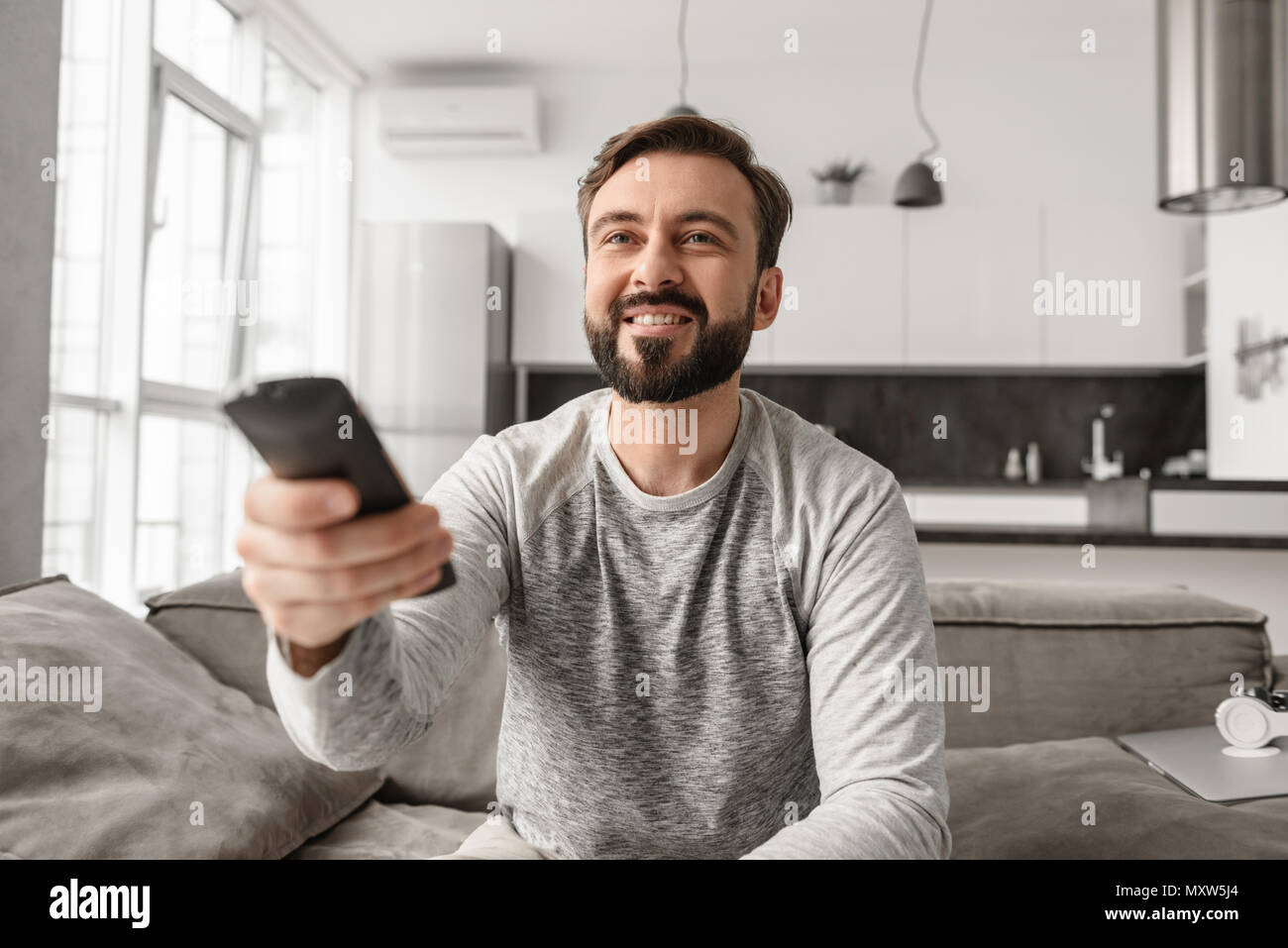Portrait of a happy young man holding TV remote control while sitting ...