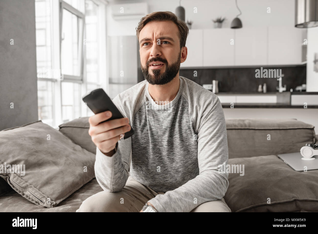 Portrait of a frustrated young man holding TV remote control while ...