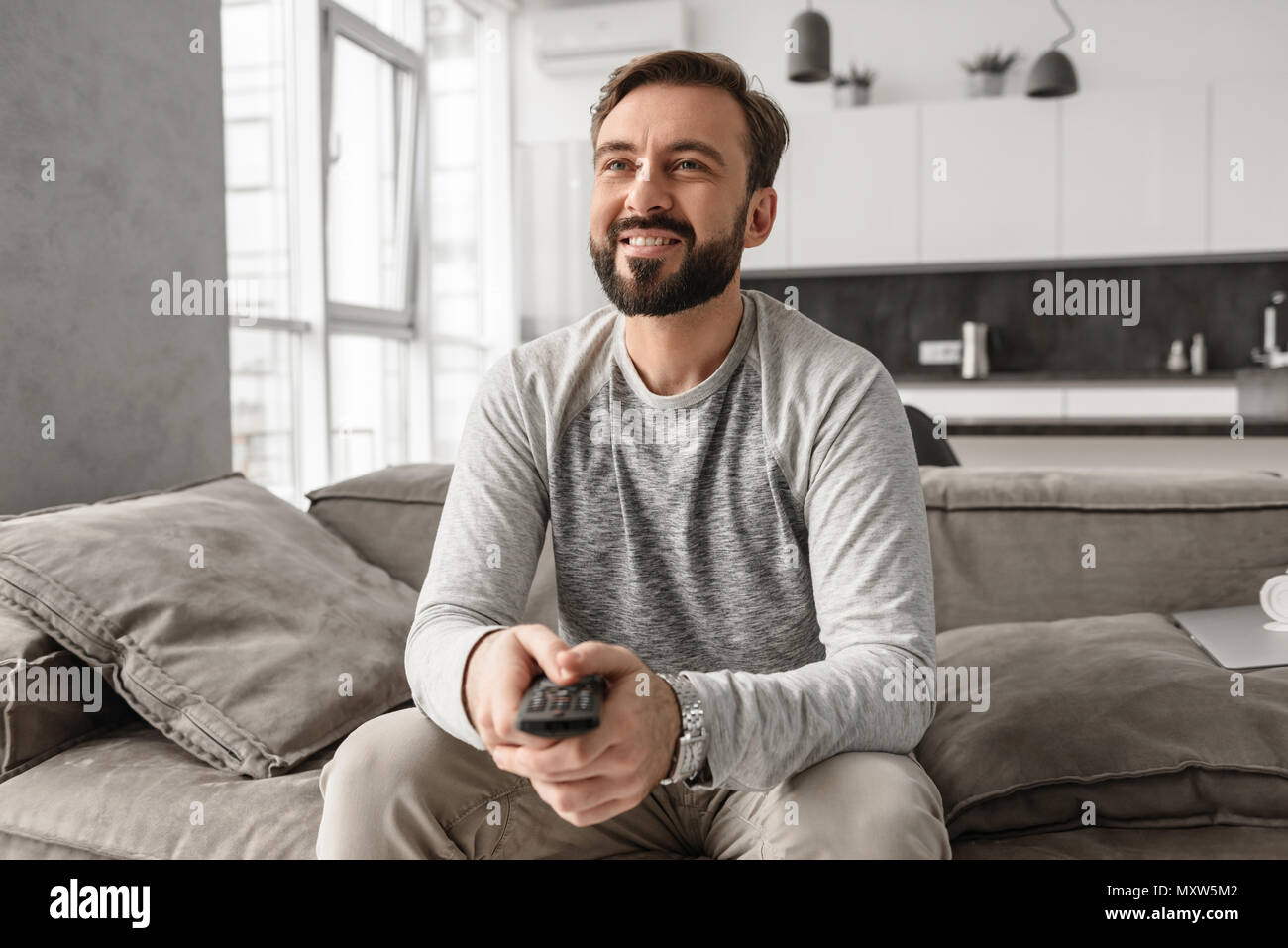 Portrait of a cheerful young man holding TV remote control while ...