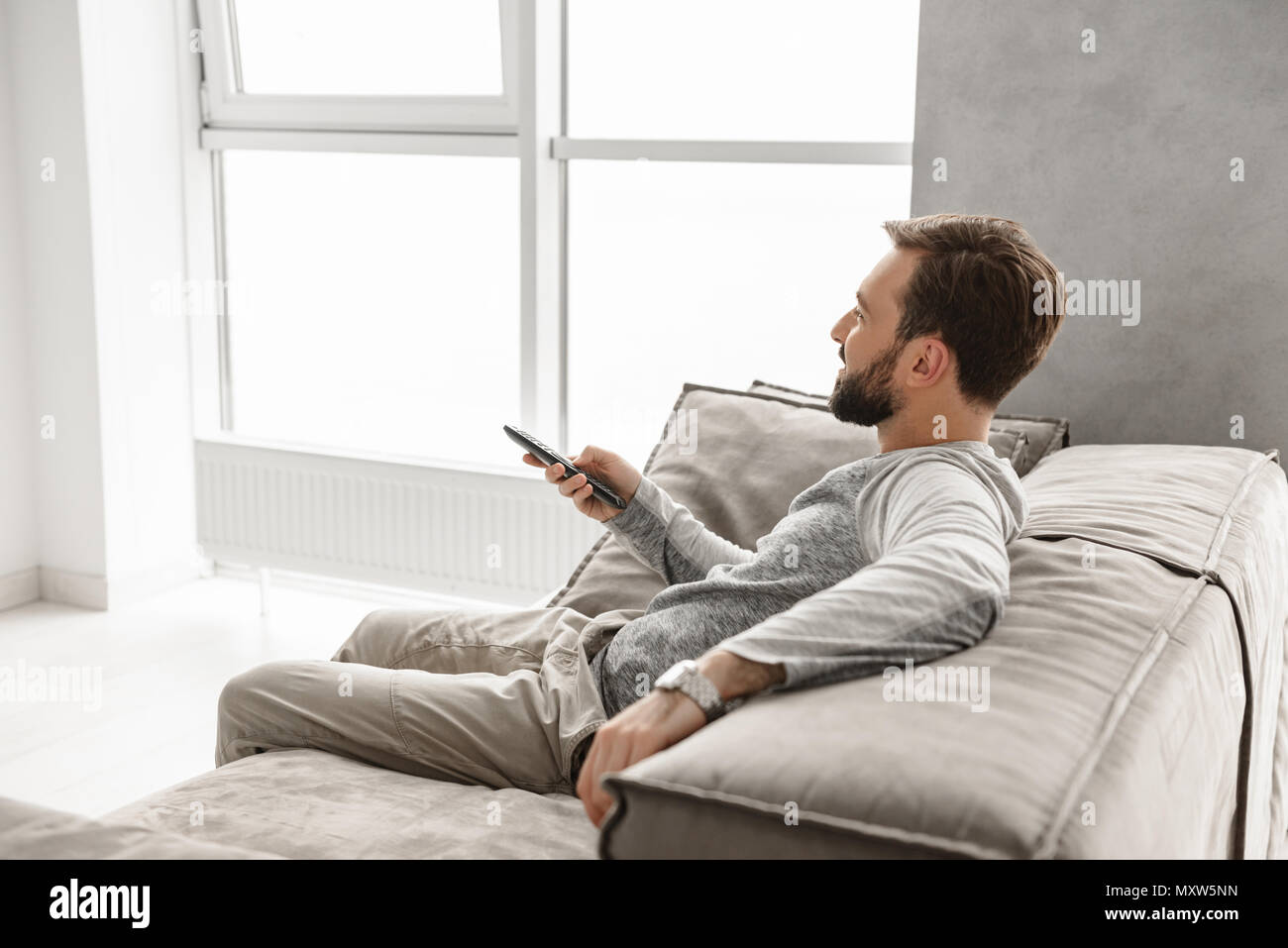 Portrait of a smiling young man holding TV remote control while sitting ...