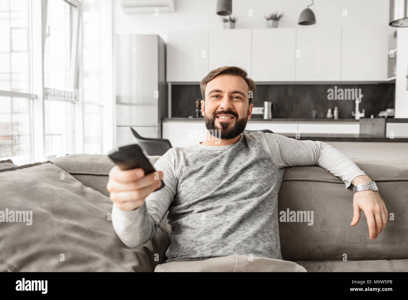 Portrait of a happy young man holding TV remote control while sitting ...