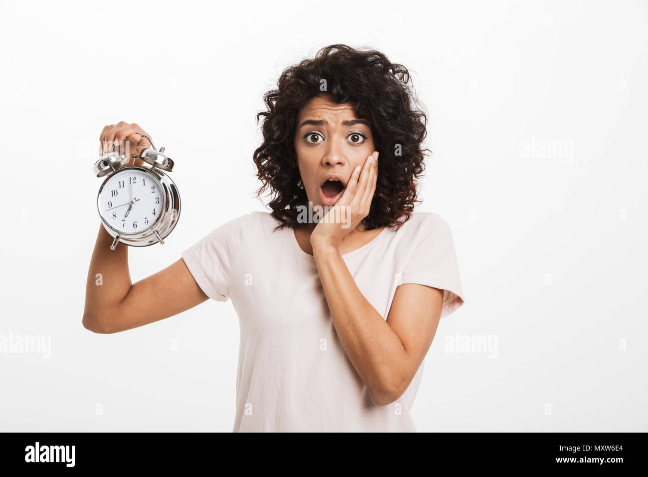 Portrait of a shocked young afro american woman holding alarm clock ...