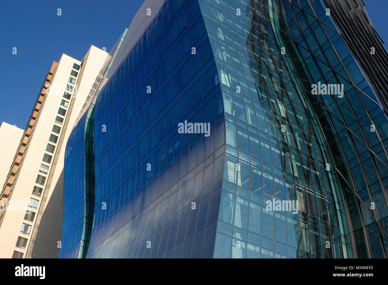 Modern curved blue corporate building next to a yellowish classical one ...