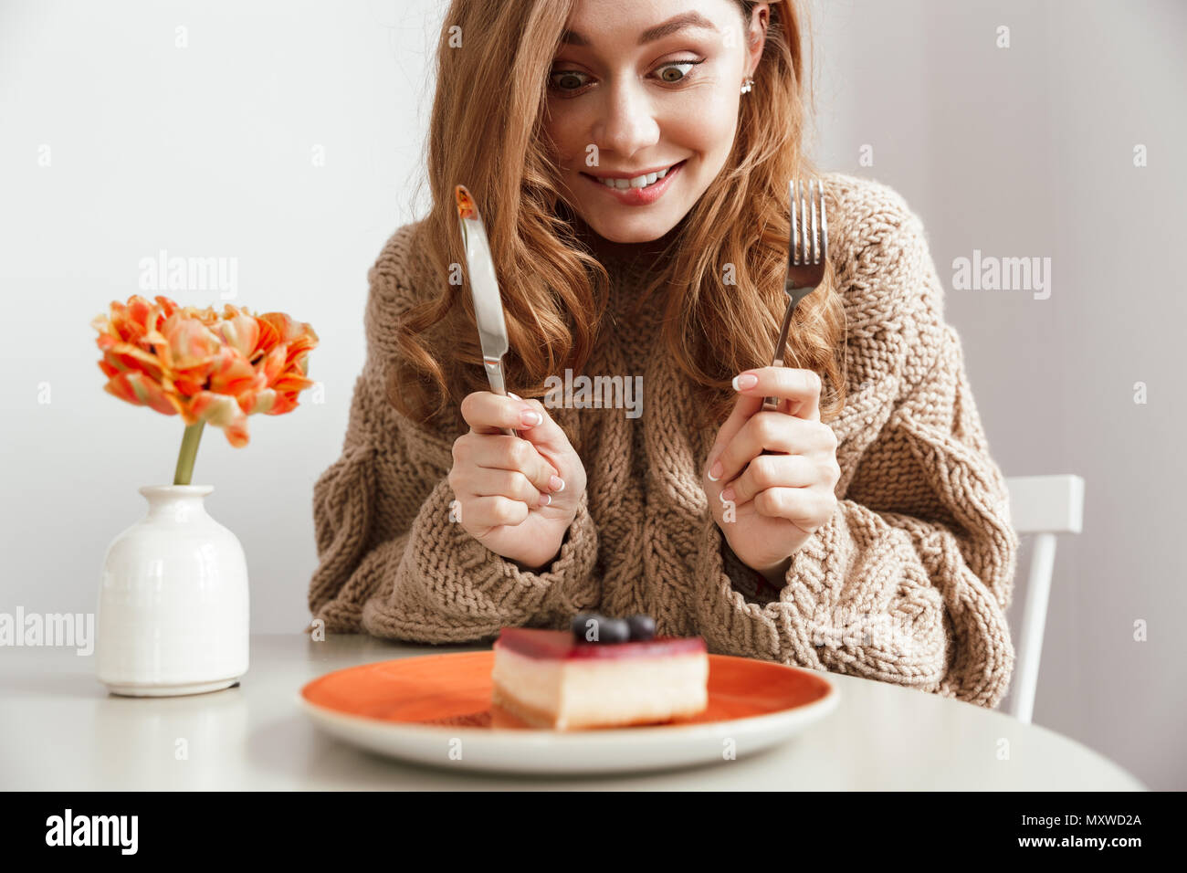Image of hungry woman sitting at table and eating cake with appetite ...