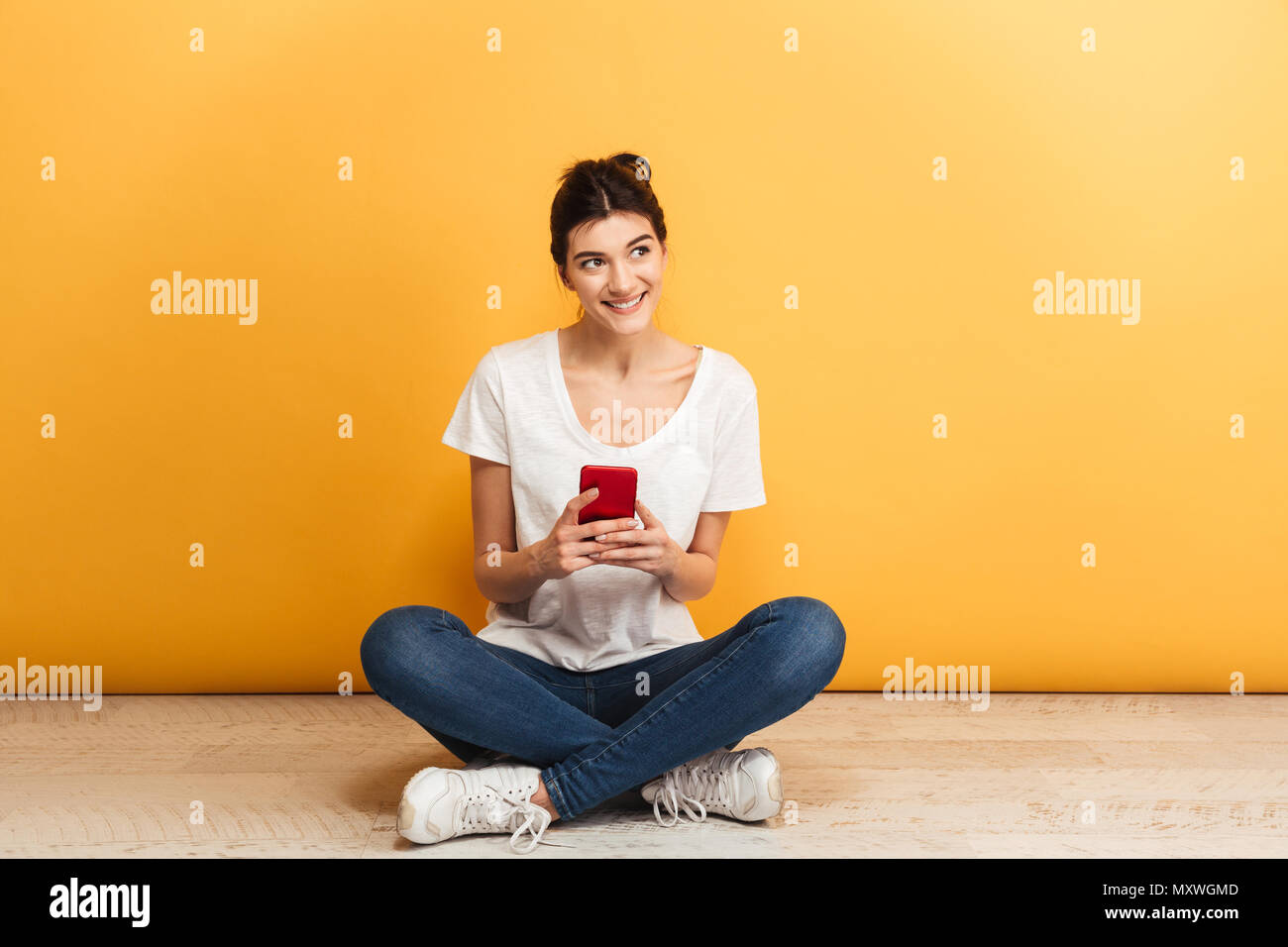 Portrait of a lovely young woman holding mobile phone while sitting ...