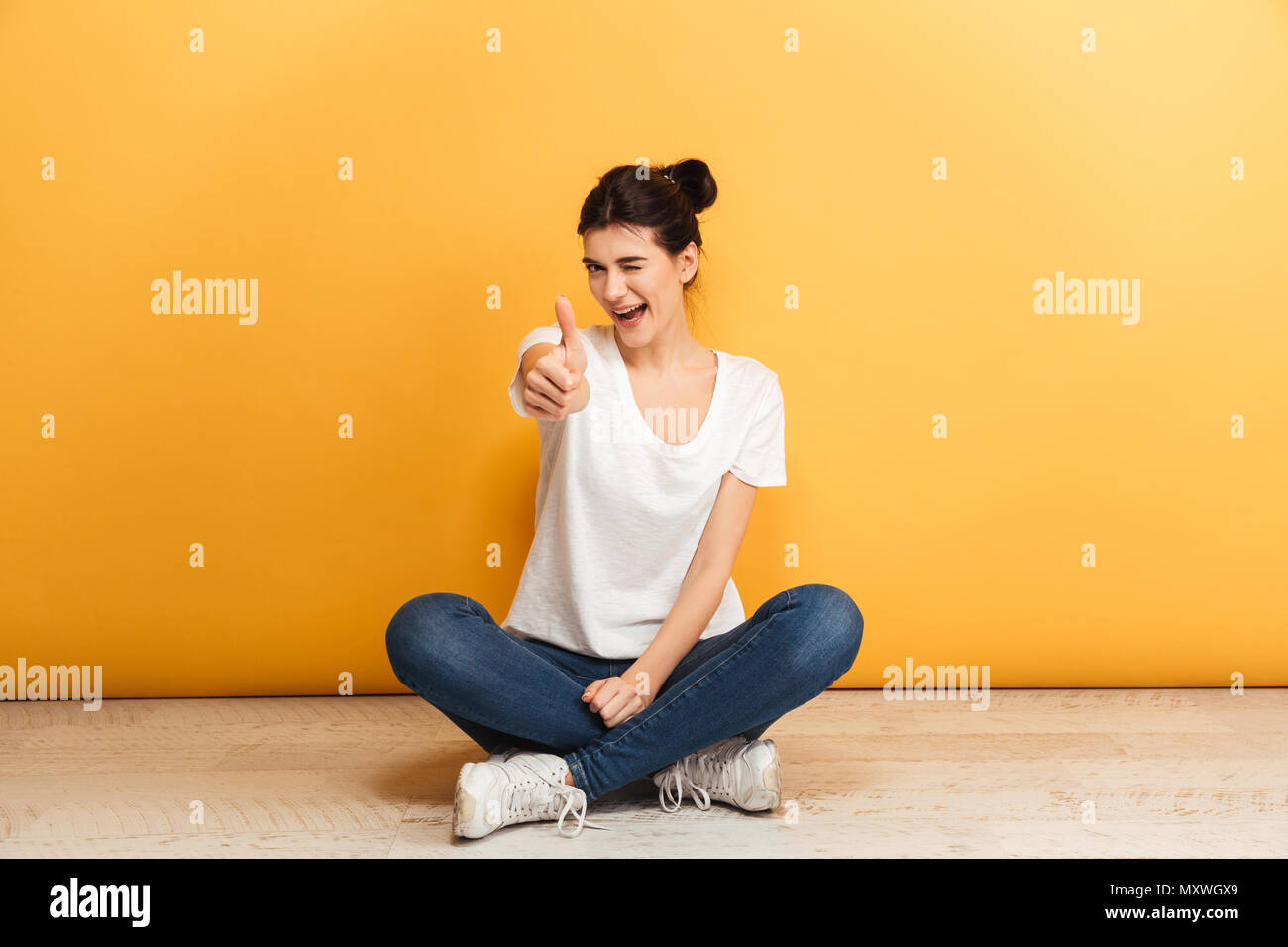 Portrait of a smiling young woman sitting with legs crossed on a floor ...