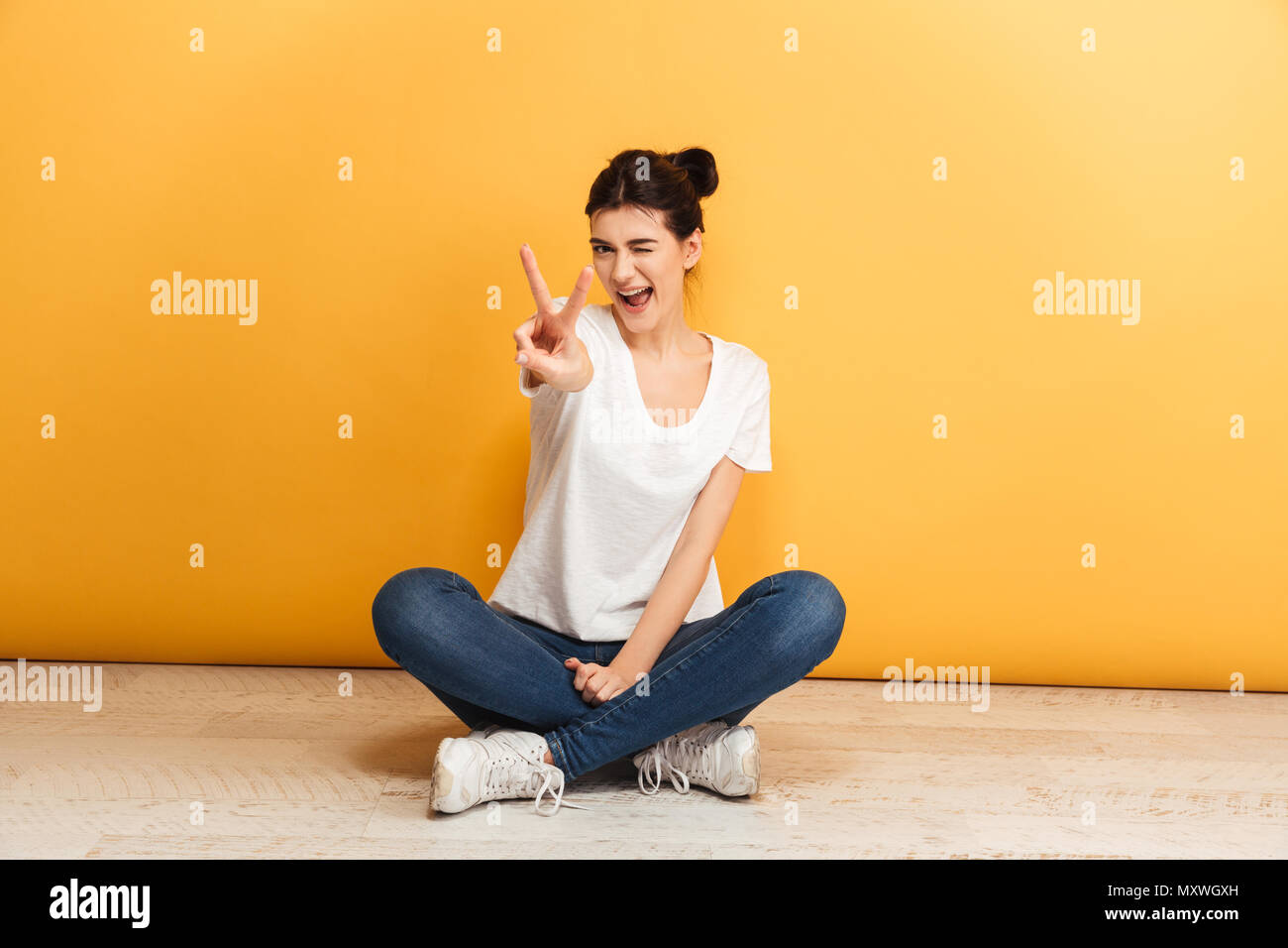 Portrait of a smiling young woman sitting with legs crossed on a floor ...