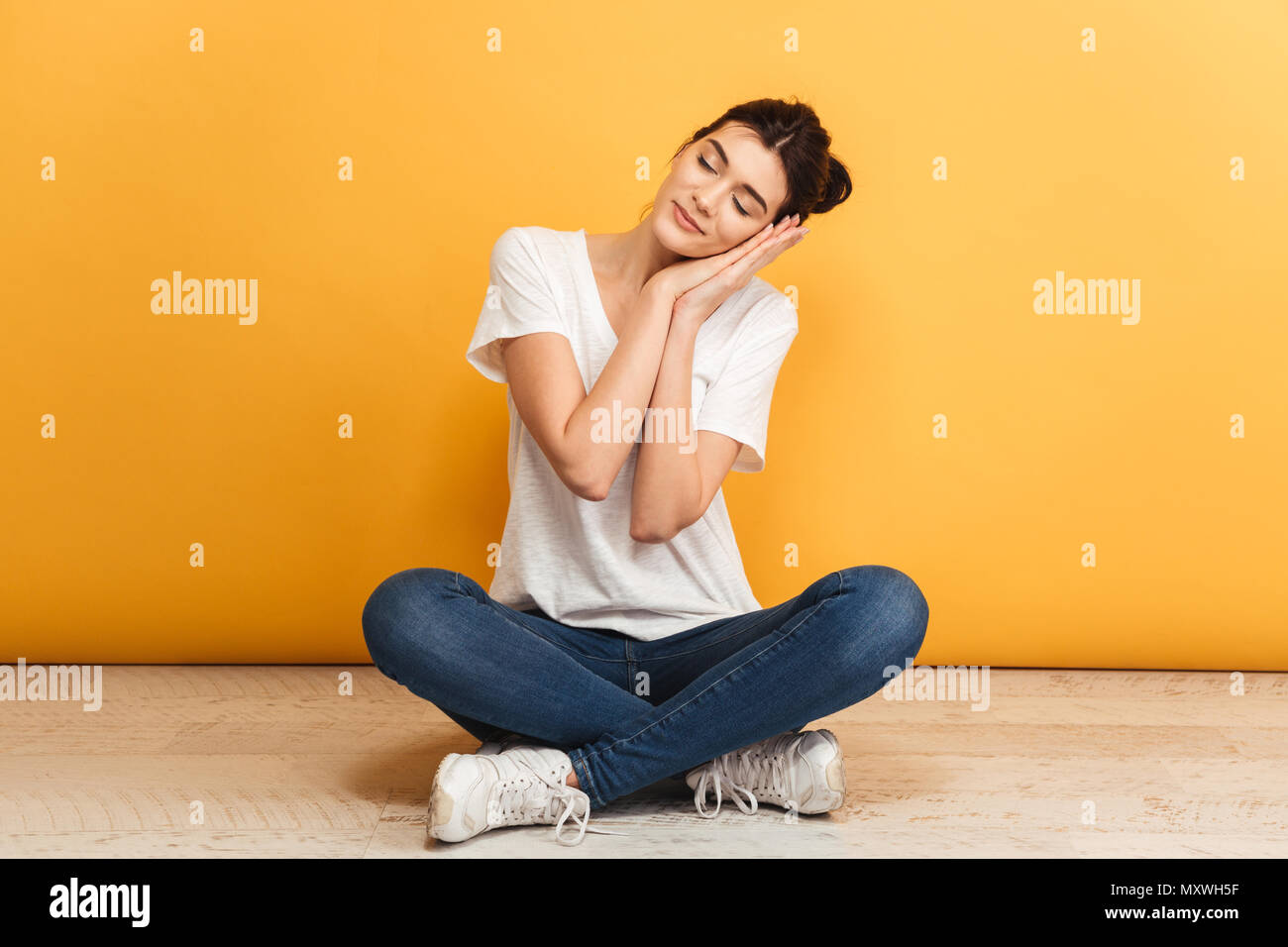 Portrait of a pretty young woman showing sleeping gesture while sitting ...