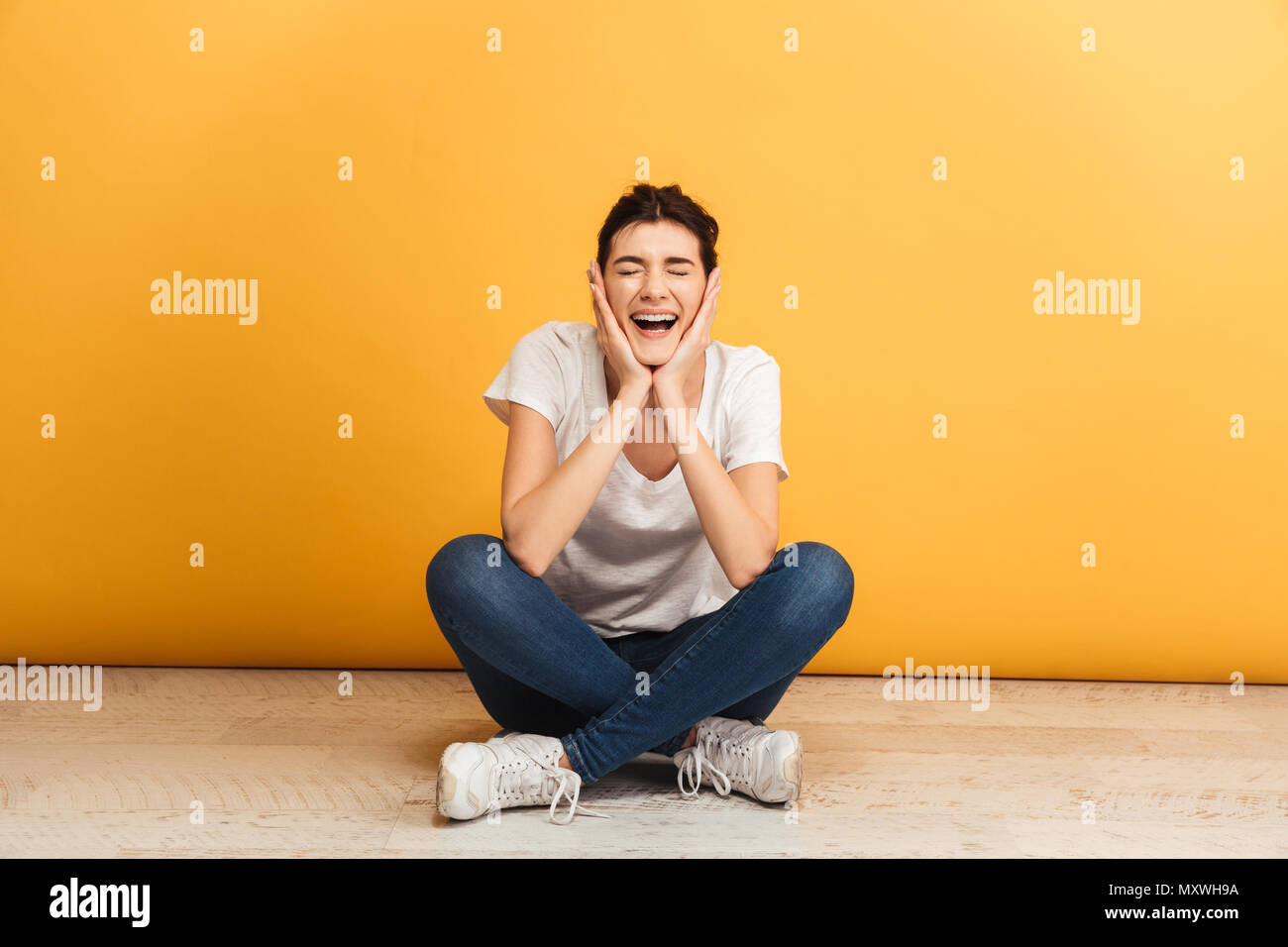 Portrait of an excited young woman sitting with legs crossed on a floor ...