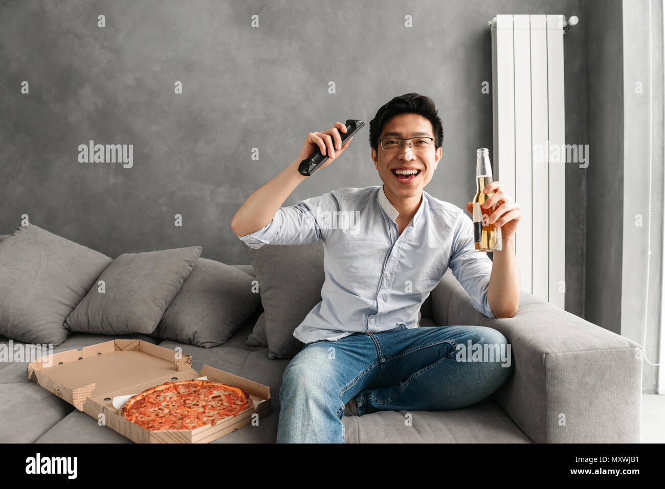 Portrait of an excited young asian man holding beer bottle and TV ...