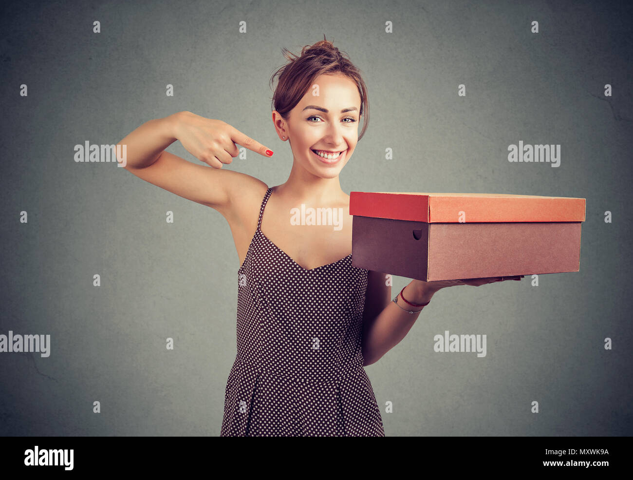 Trendy happy woman holding box and pointing at it with smile while ...