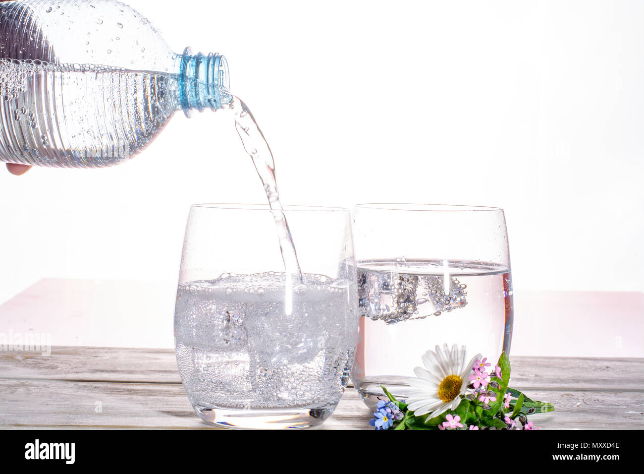Pouring of sparkling soda mineral drink water in glasses with ice cubes close up copy space ...