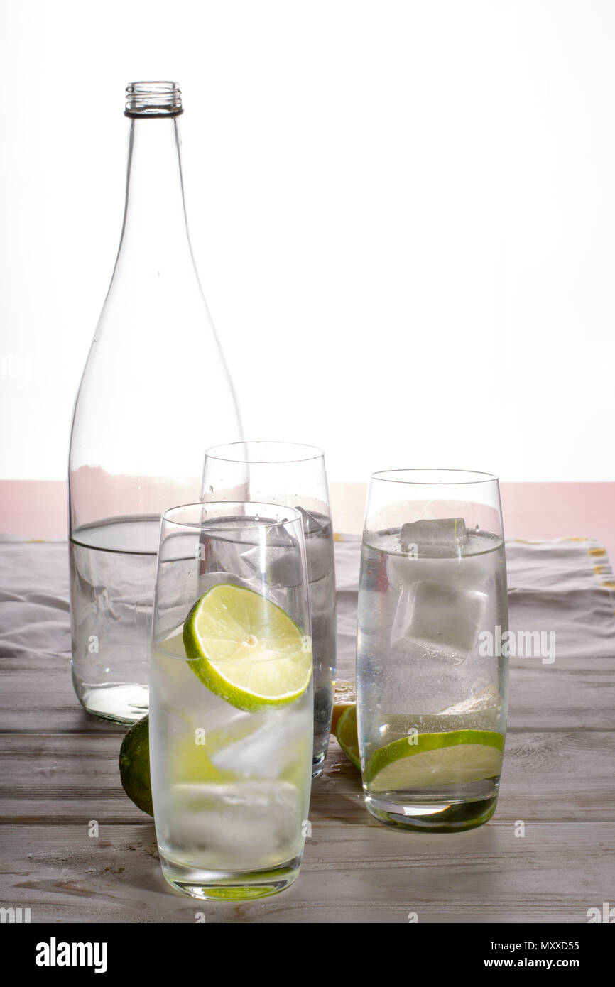 Stil mineral drink water in glass bottle served with three glasses with ice cubed, lime and ...
