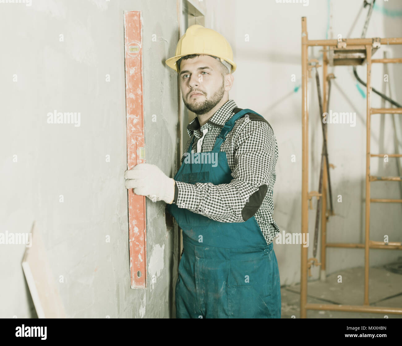 Repairman in helmet is measuring wall with level Stock Photo - Alamy