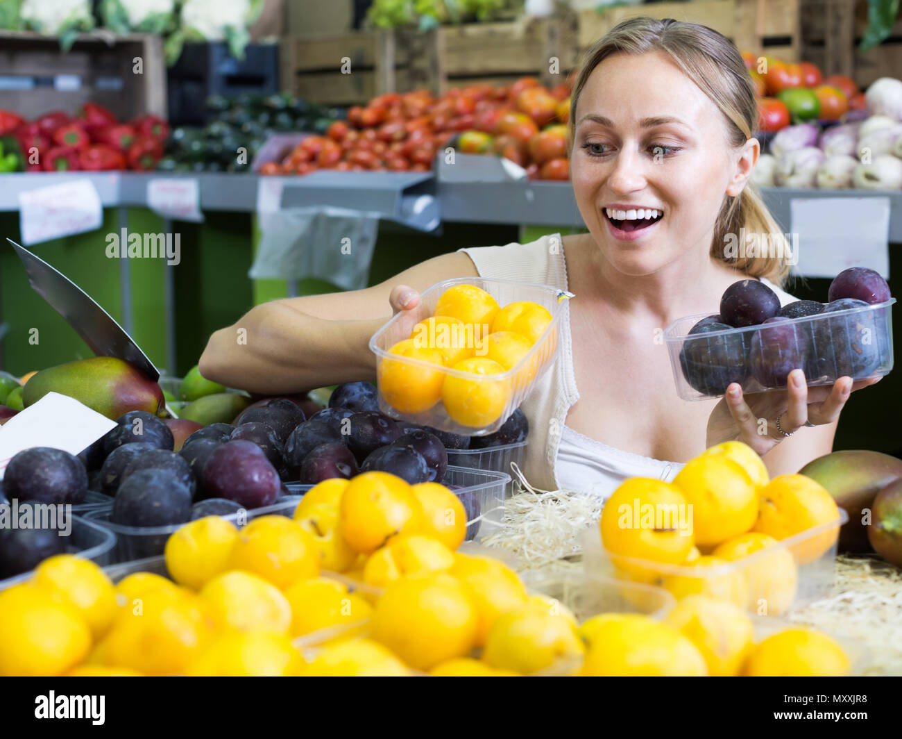 joyful young female customer choosing plums on fruit market Stock Photo ...