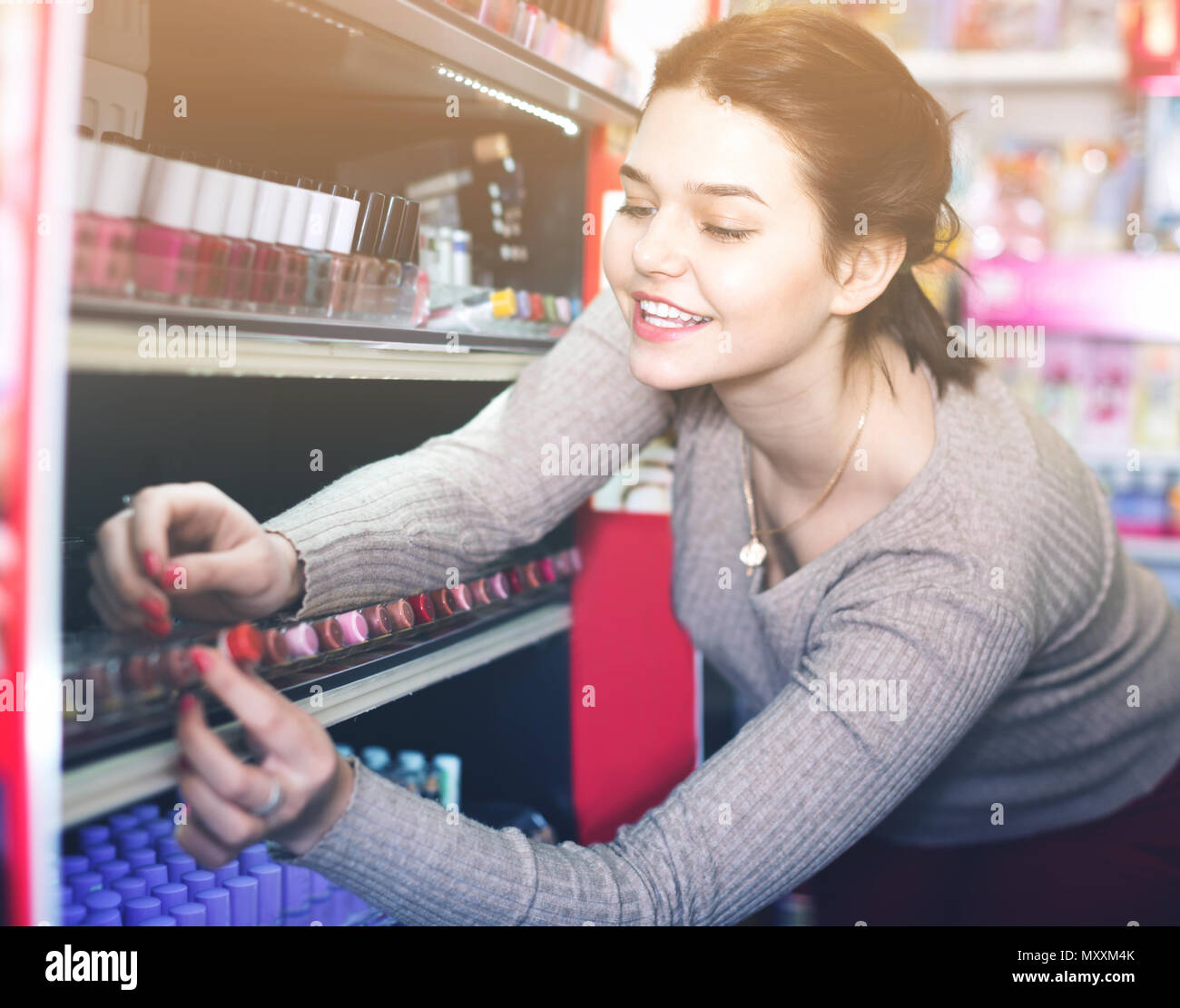 Cheerful positive woman customer browsing rows of lipstick in cosmetics ...