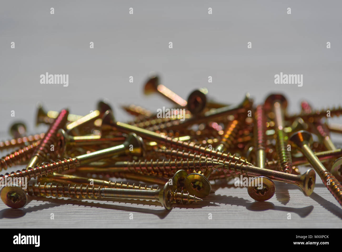 Close-up photo of a pile of yellow shiny screws on wooden background ...
