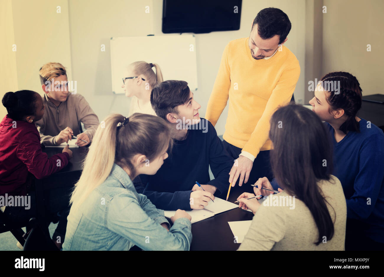 Positive classmates and male teacher working in groups to complete task ...