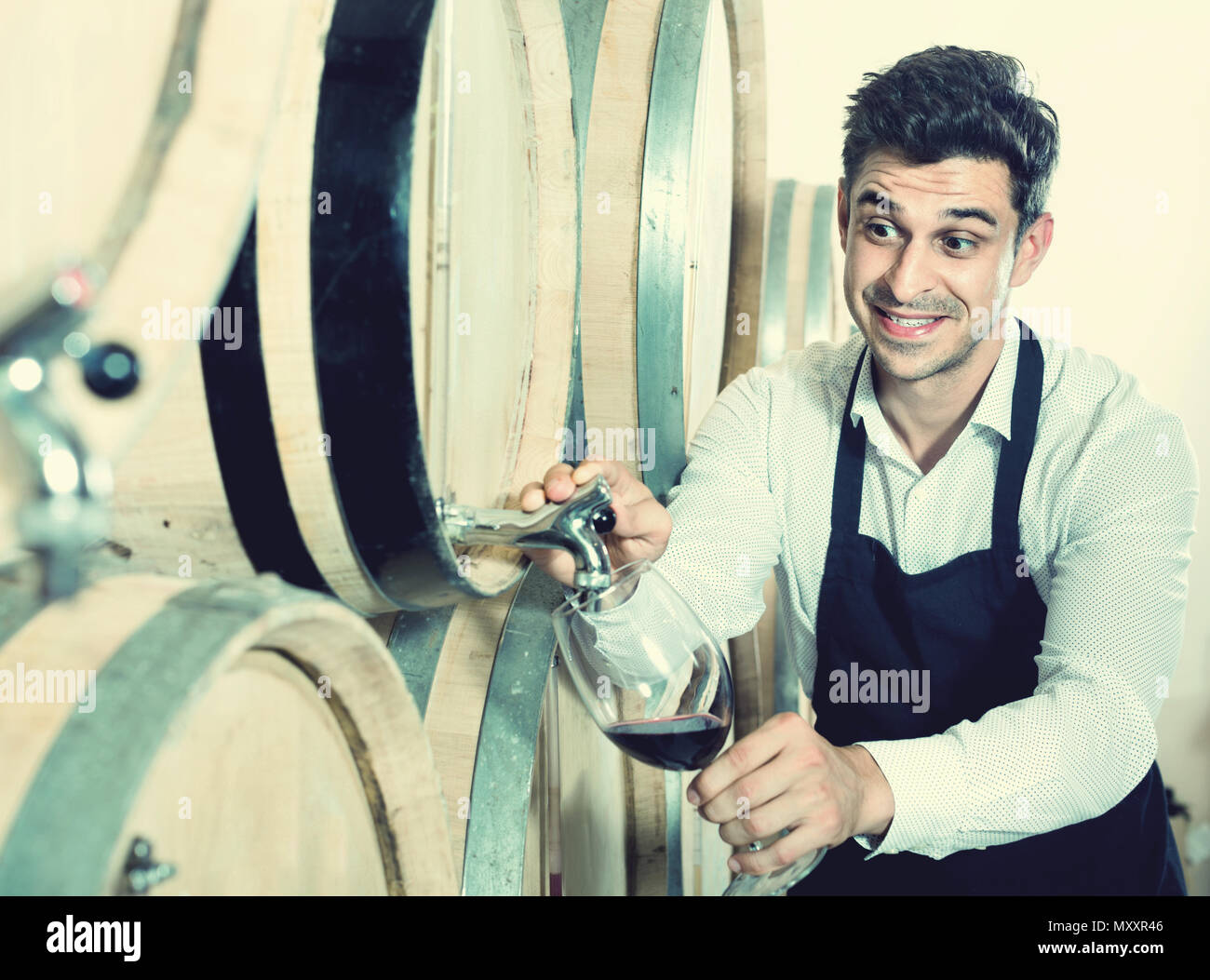 Glad man in uniform pouring red wine into glass in alcohol section with ...