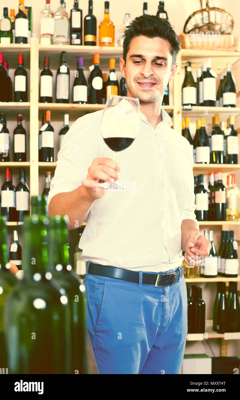 portrait of smiling american man tasting wine sample in glass in shop ...