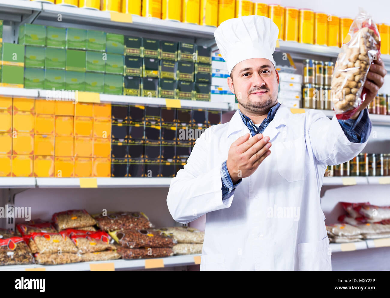 Happy shop staff offers food products and showing filled shelves behind ...