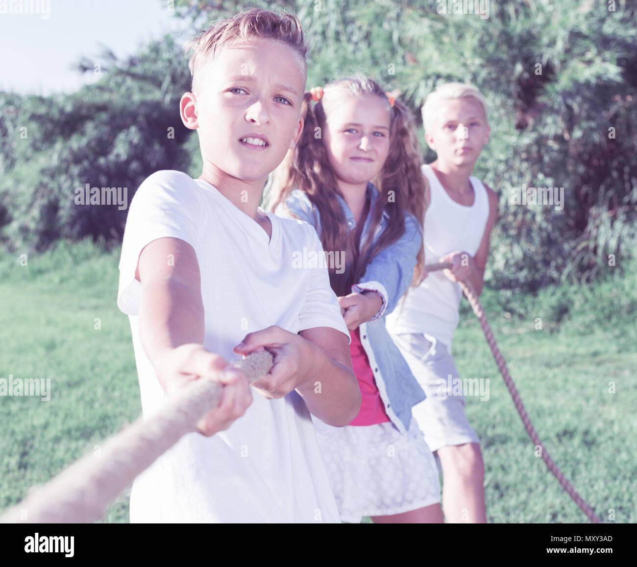 Group of laughing children having fun together outdoors pulling rope ...