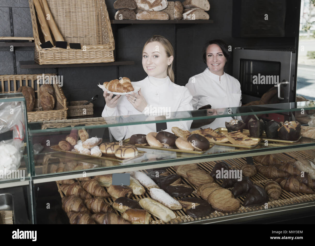 Happy women dressed as cooks showing their desserts in the pastry shop ...