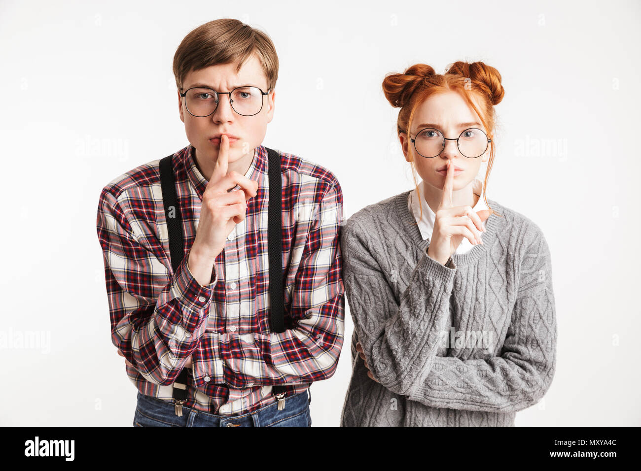 Serious couple of school nerds showing silence gesture isolated over white background Stock ...