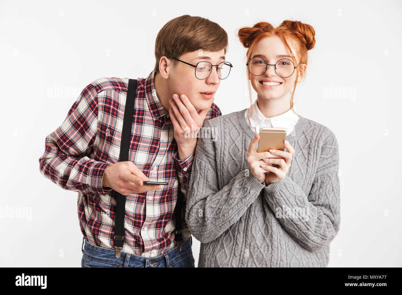 Happy couple of school nerds using mobile phones isolated over white ...