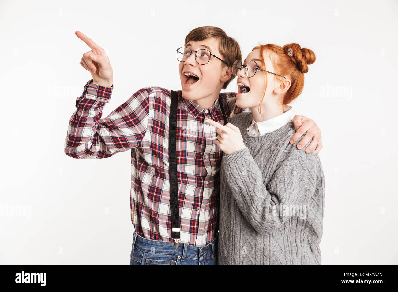 Cheerful couple of school nerds pointing fingers away at copy space ...