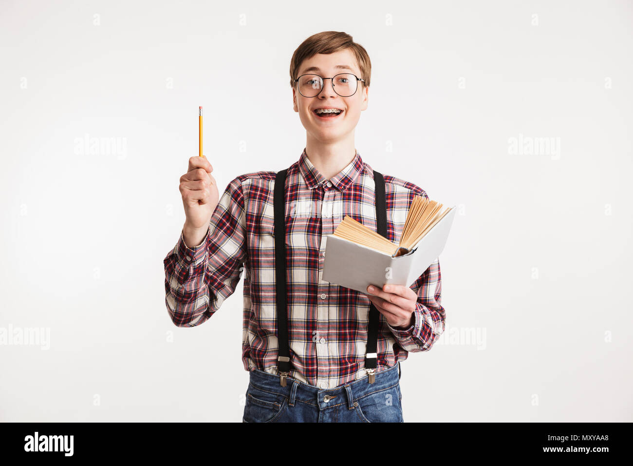 Portrait of a smiling young school nerd guy holding book and poinitng ...