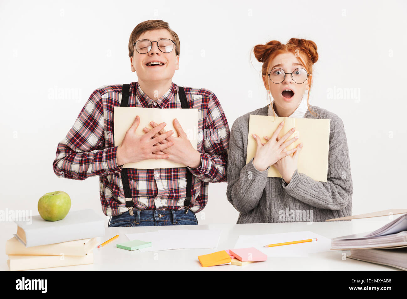 Happy couple of school nerds hugging books while sitting at the desk ...