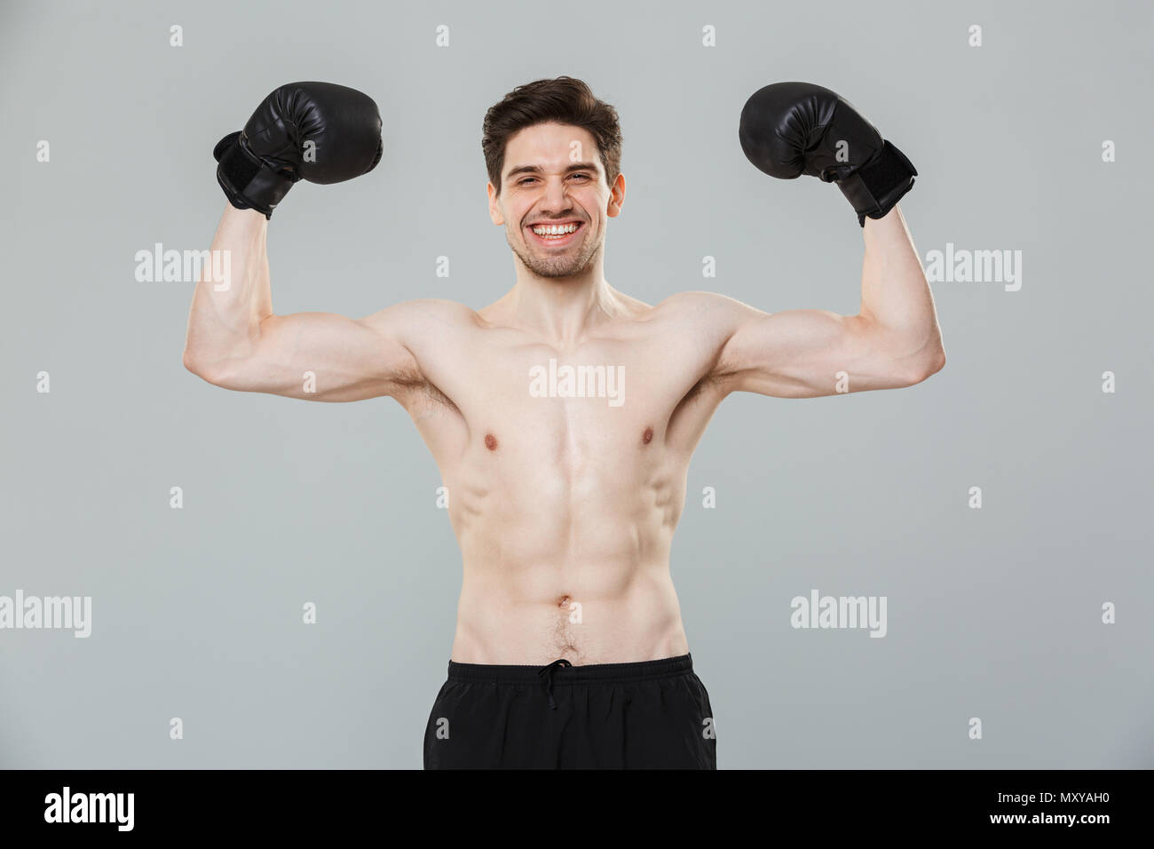 Portrait of a happy young sportsman flexing biceps while wearing boxing ...