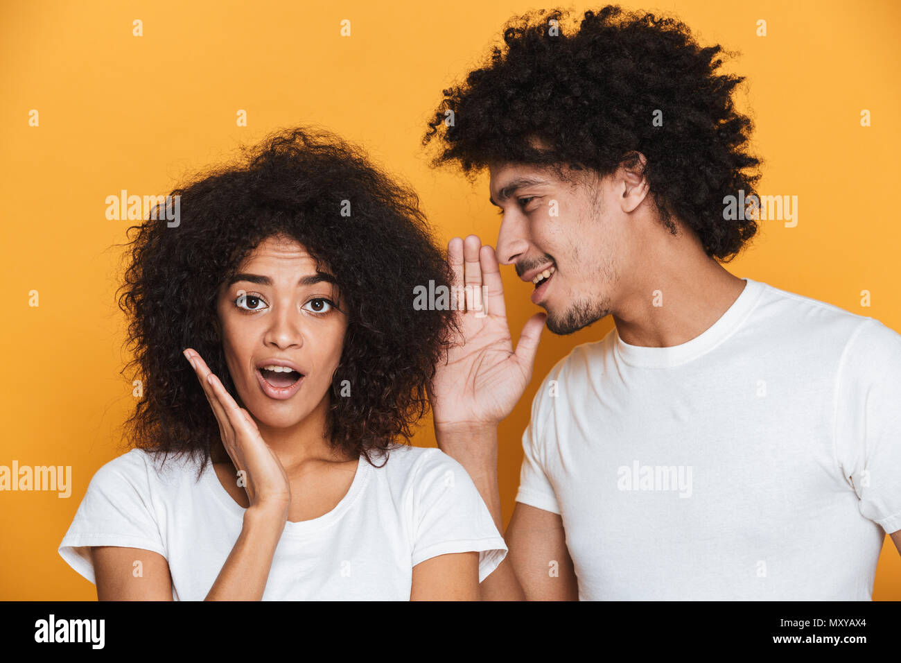 Portrait of a surprised young afro american couple telling secrets ...