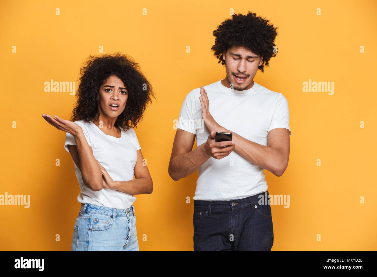 Portrait of a confused afro american couple with mobile phone isolated ...