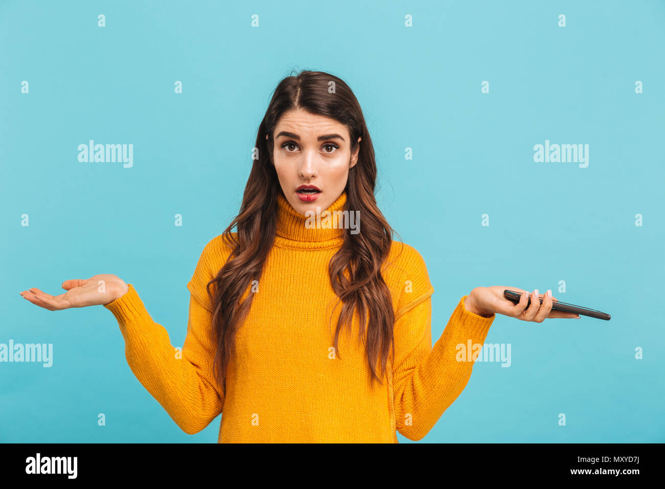 Portrait of a confused young girl in sweater holding mobile phone and ...