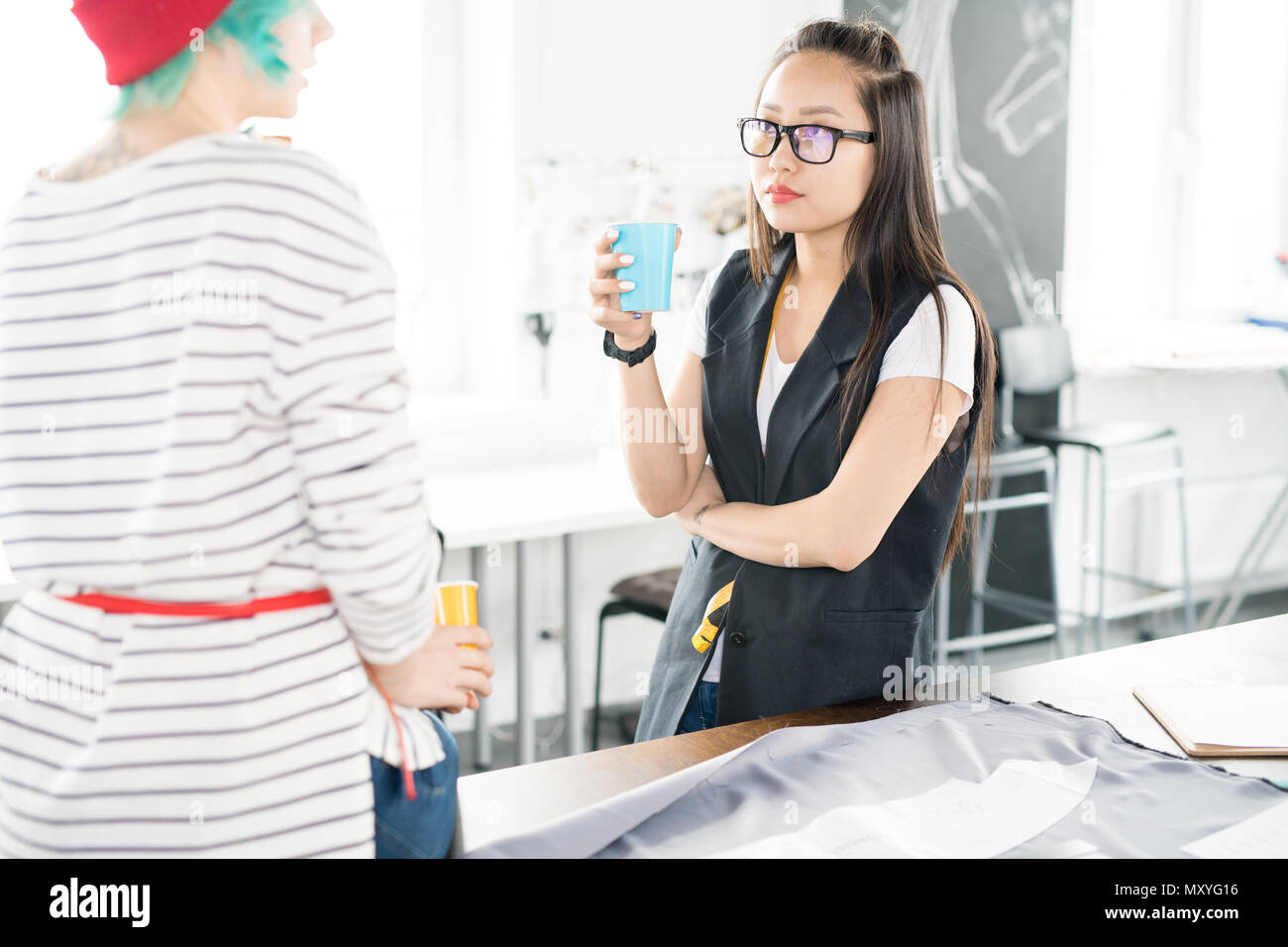 Portrait of Asian fashion designer chatting with colleague during ...